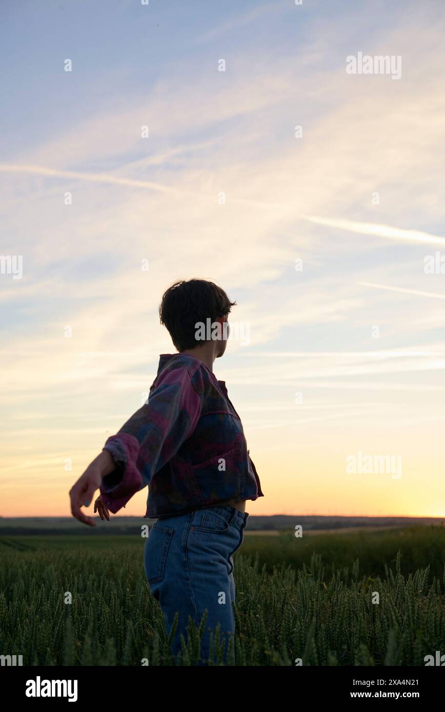 Person standing in a field at sunset, looking into the distance with a ...