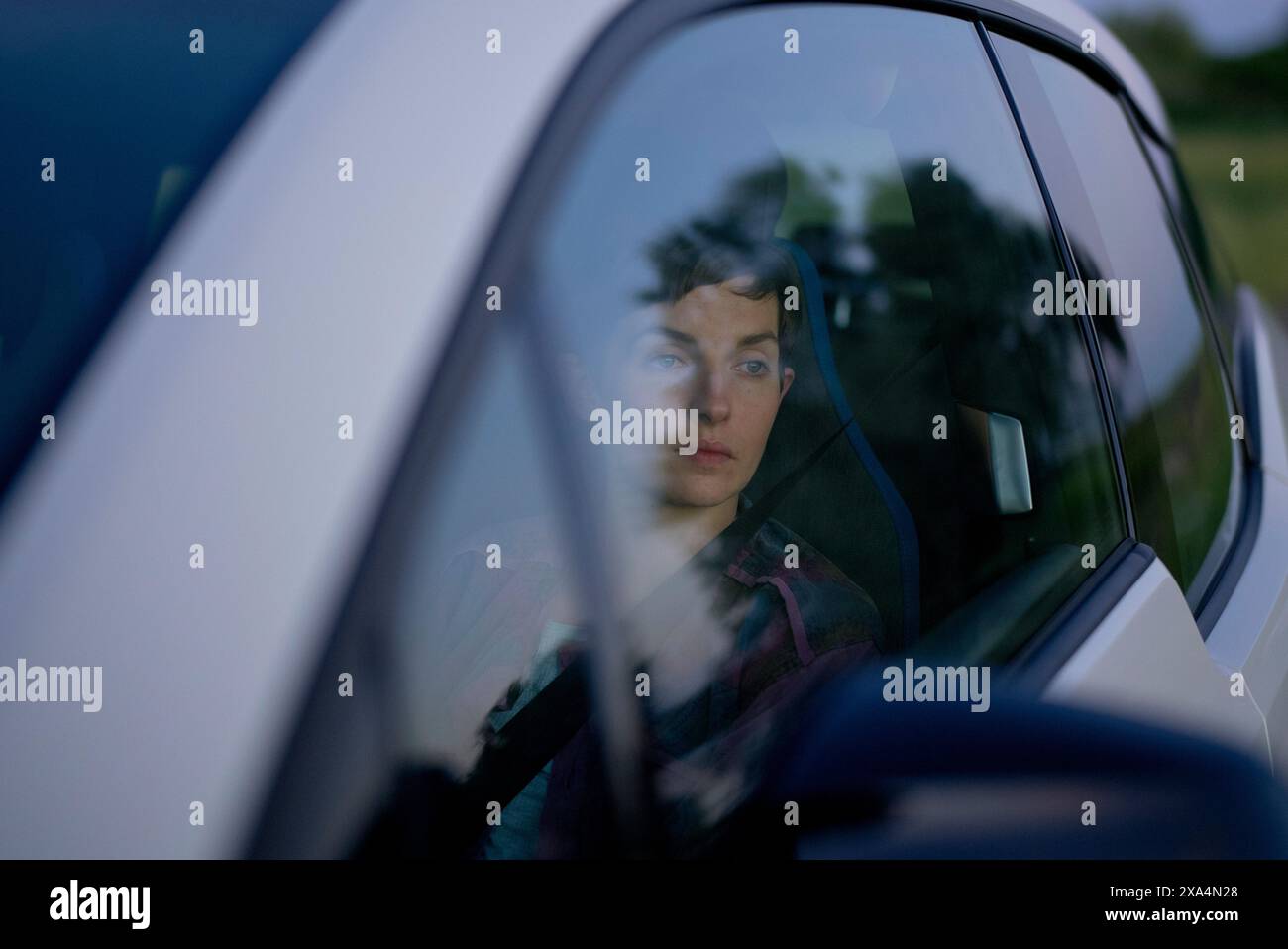 A young woman is gazing outside from the passenger seat of a vehicle ...