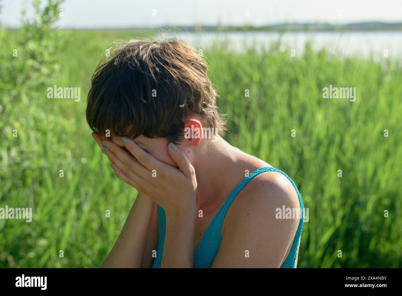 A young woman is sitting outdoors with their face in their hands ...