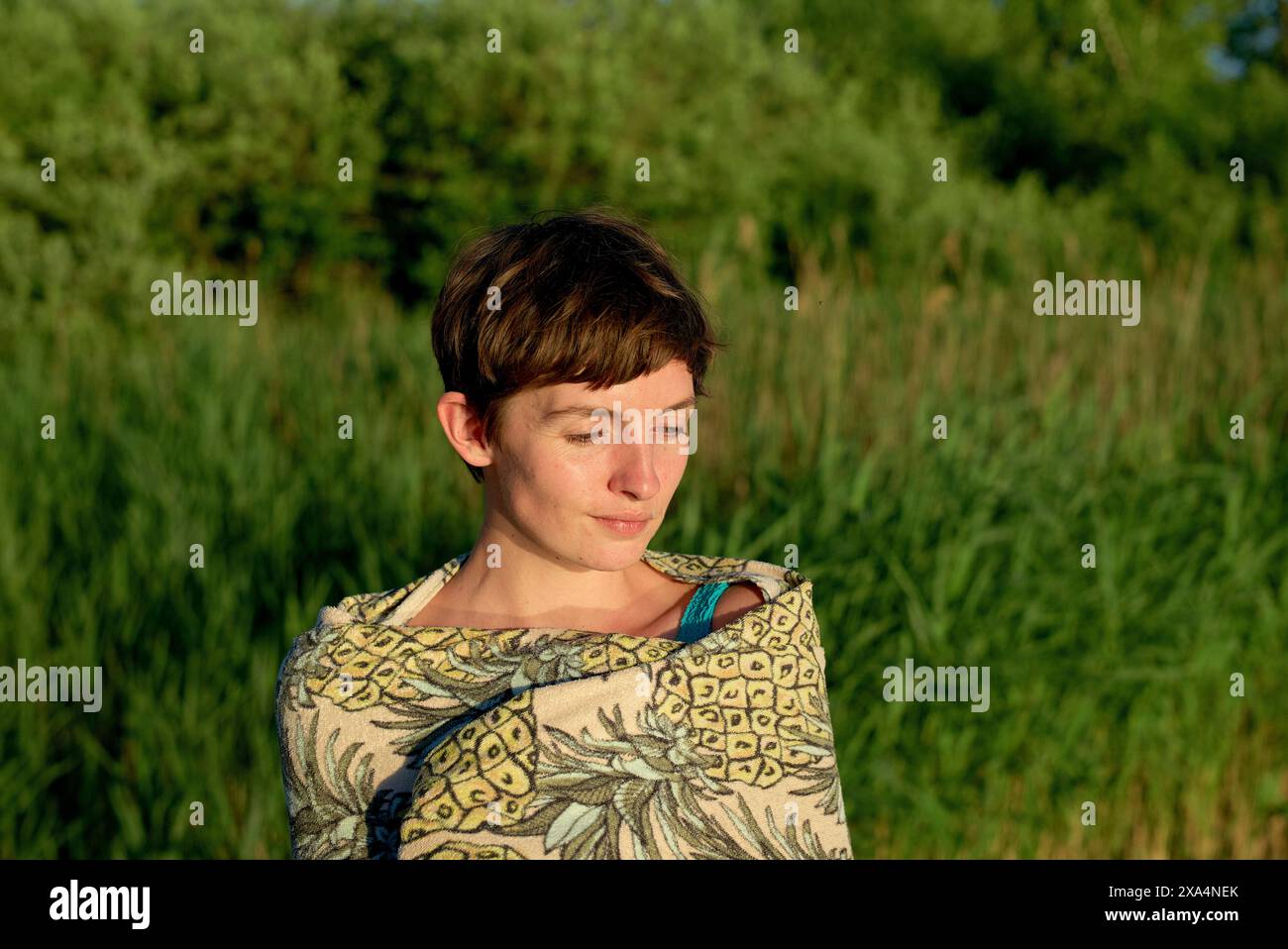 A young woman with a pixie haircut is outdoors with eyes closed and a ...