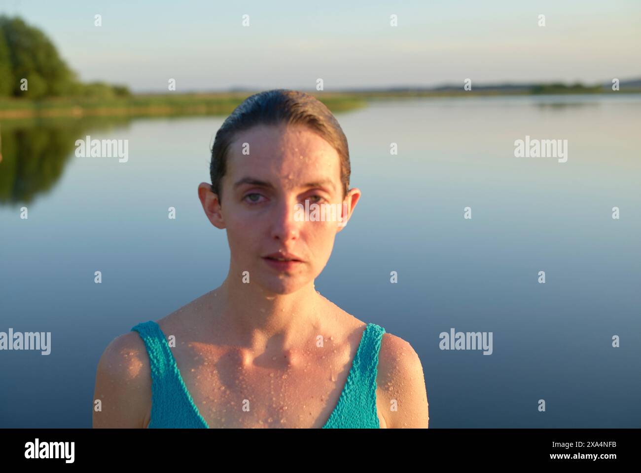 A close-up of a woman with wet skin and hair, wearing a blue tank top, standing in front of a ...