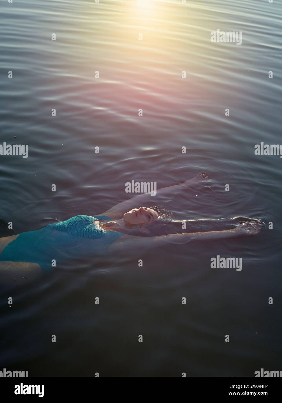 A young woman is floating peacefully on their back in calm water under ...