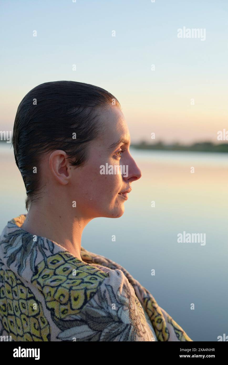 A young woman with a serene expression is looking out over a calm body ...