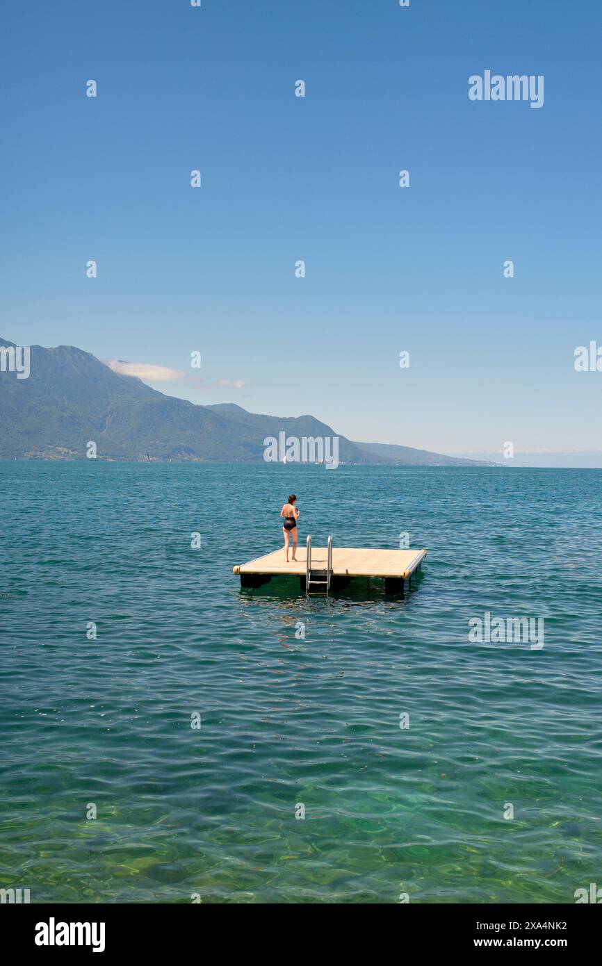 A person stands alone on a floating dock surrounded by clear blue water ...