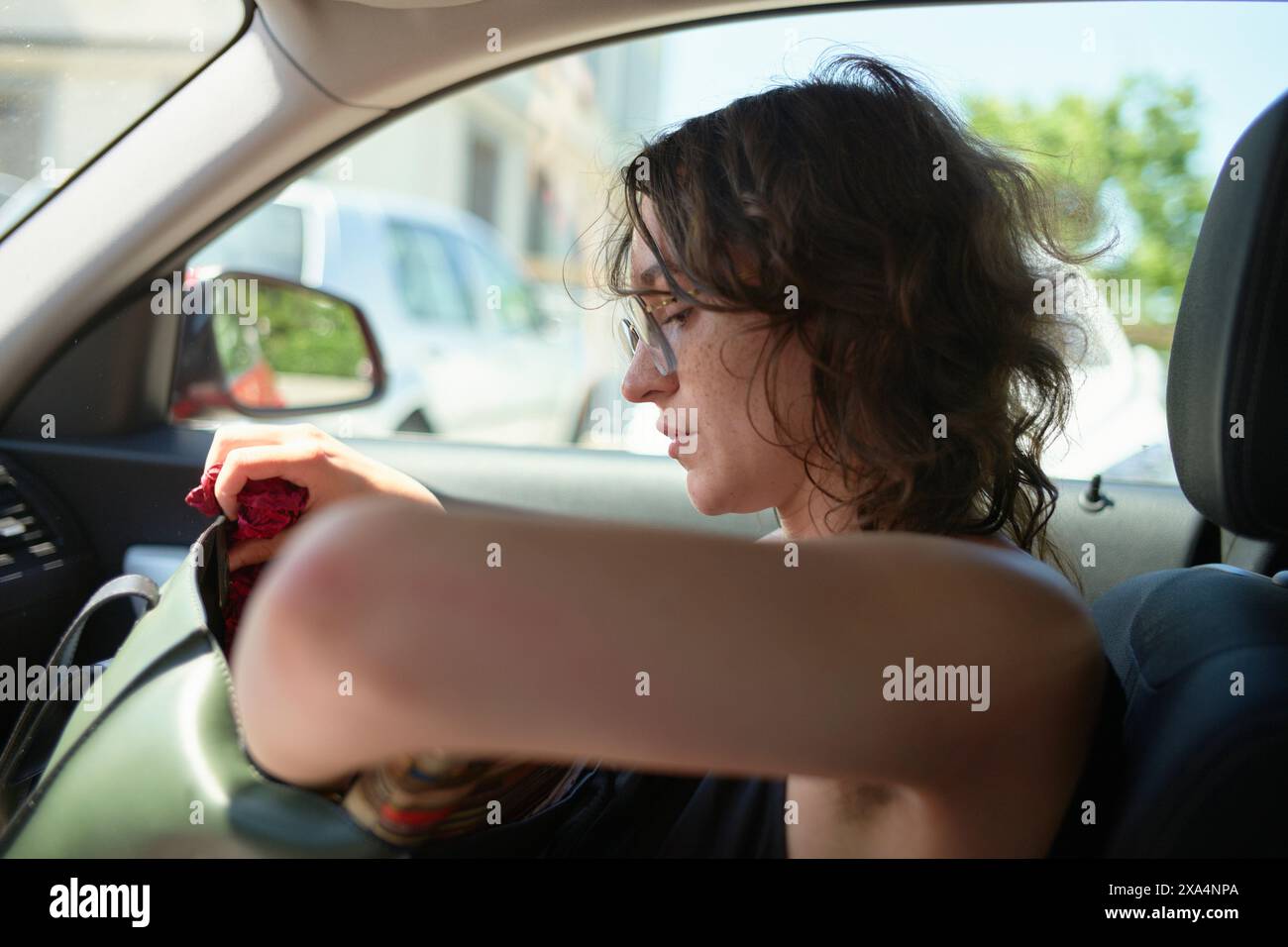 A woman is sitting in the driver's seat of a car, resting her arm on ...