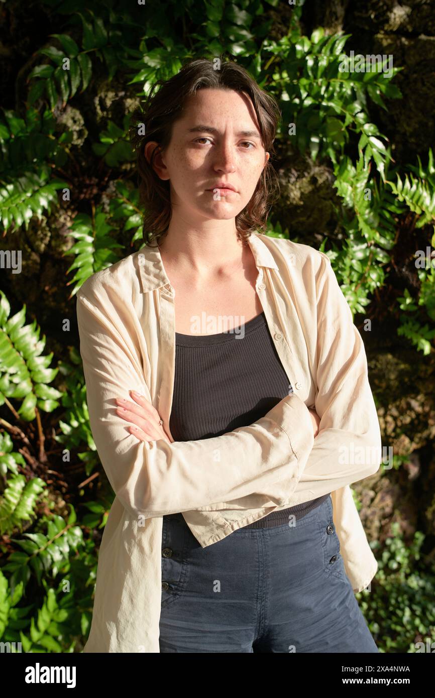 A woman is standing outdoors with her arms crossed, wearing a beige ...