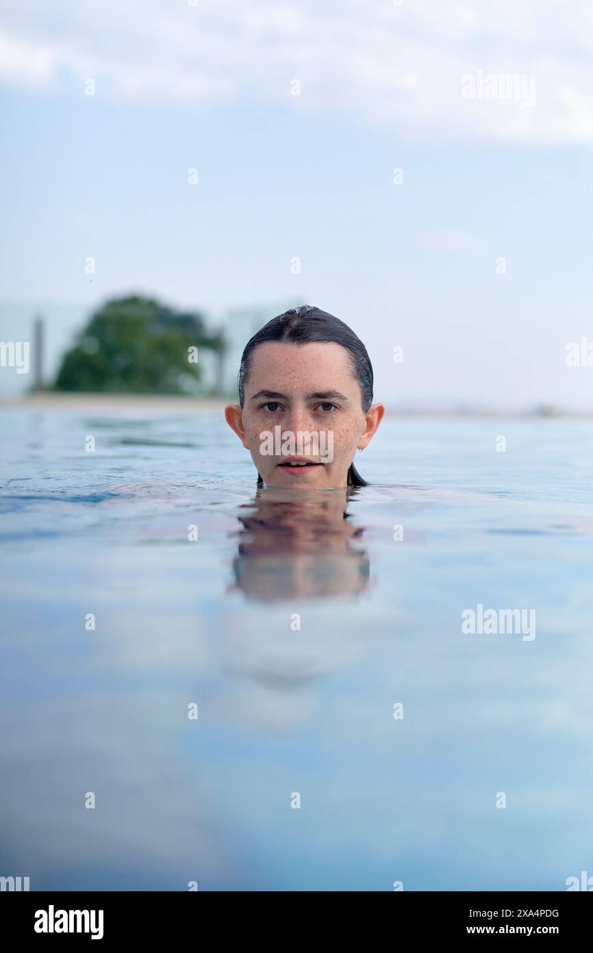 A young woman is submerged in water up to their neck, with their head ...
