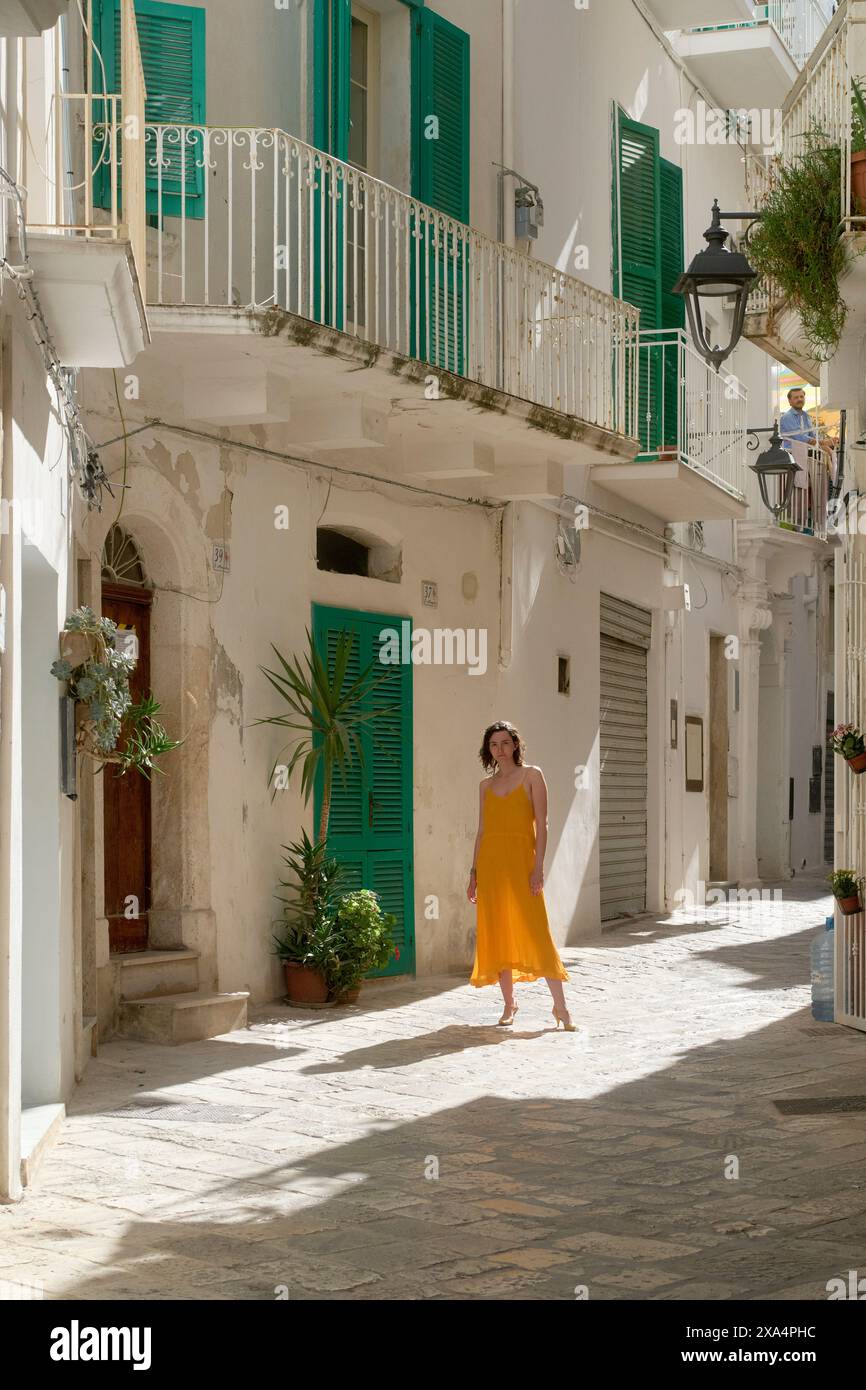A woman in a flowing yellow dress strolls down a quaint, sunlit street ...