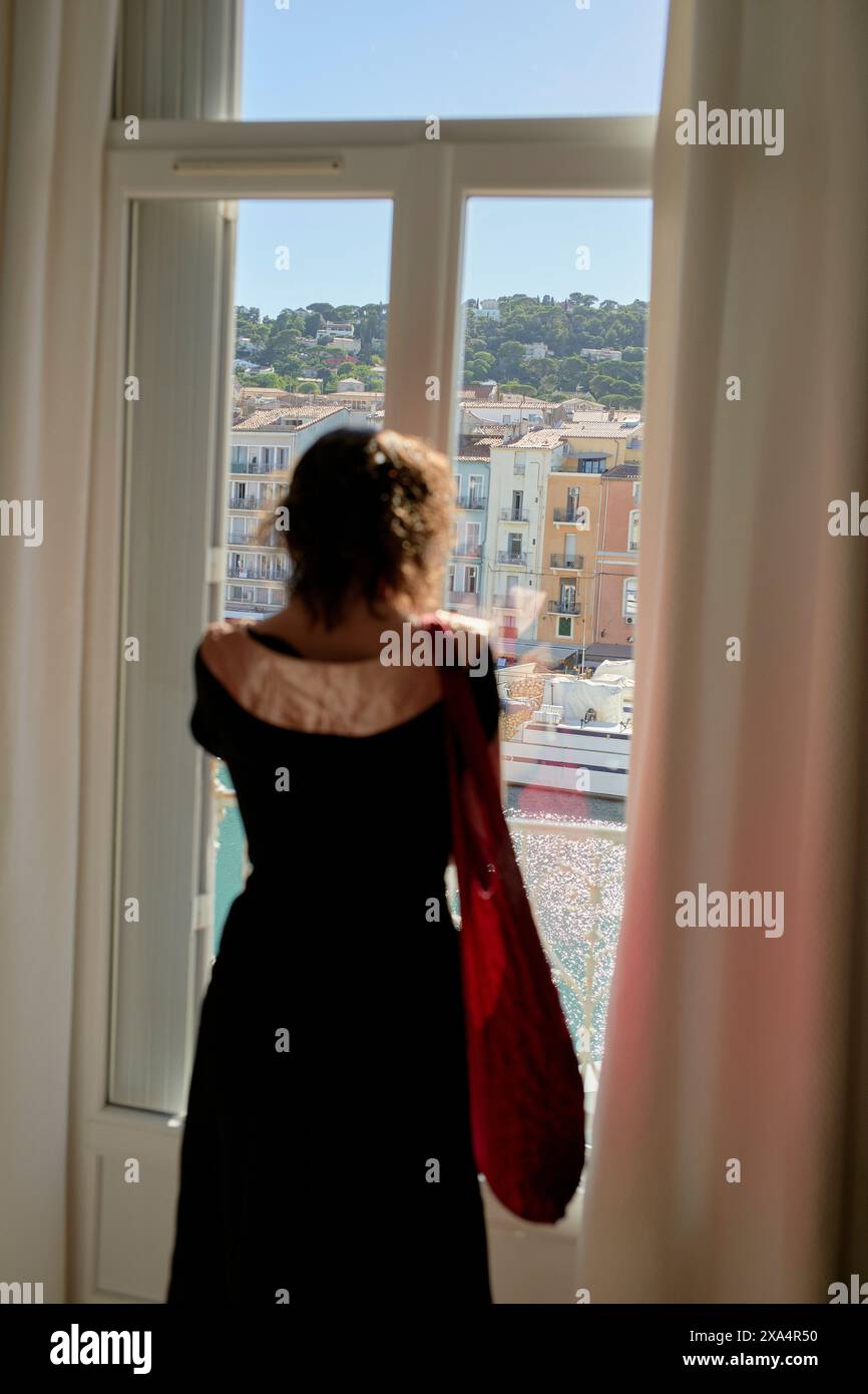 A person standing by an open window, overlooking a cityscape with ...