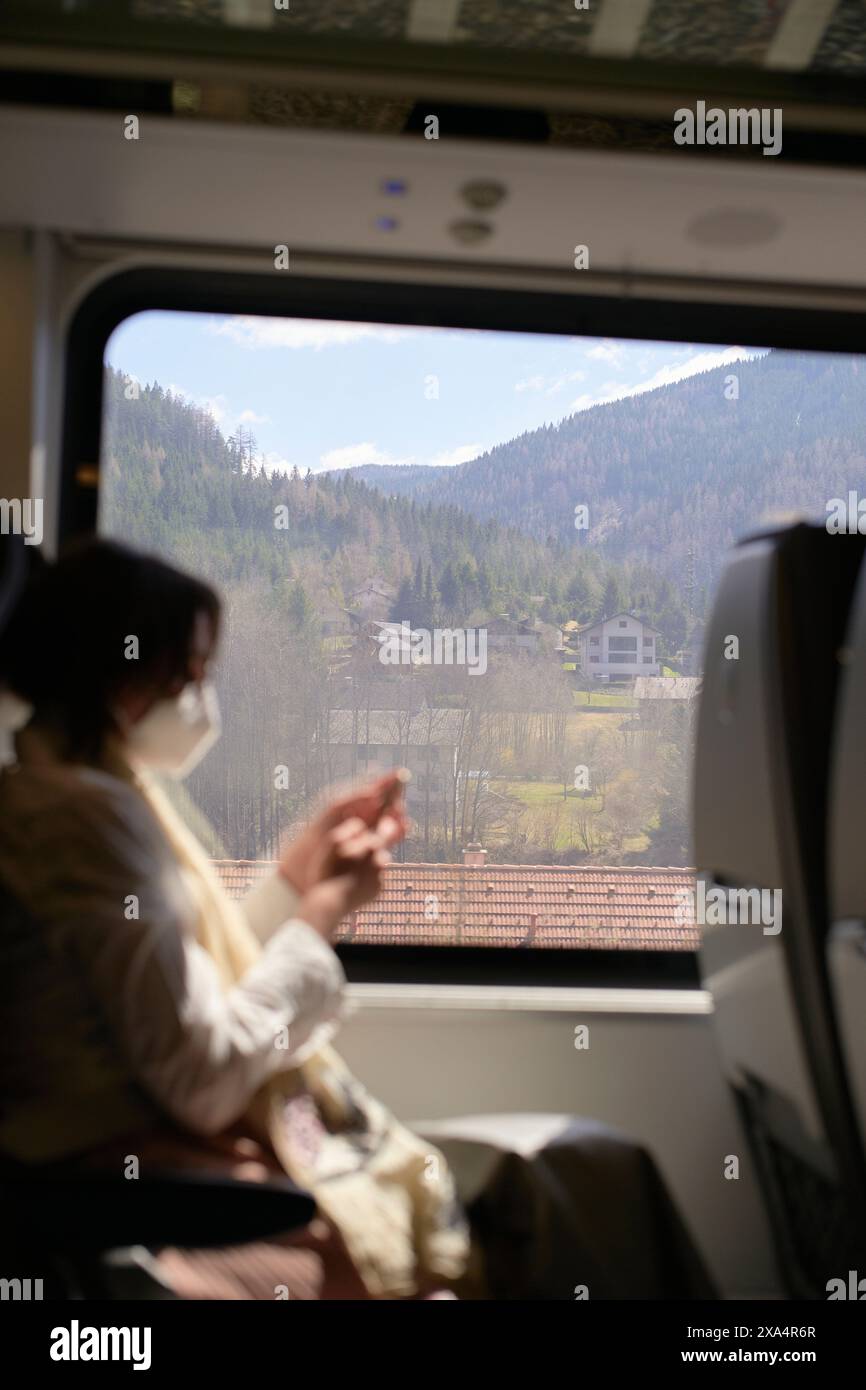 A person is seated on a train, looking out the window at a scenic ...