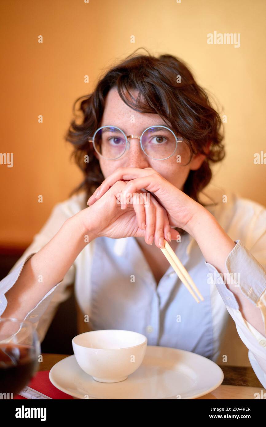 Woman with glasses resting chin on hands at a restaurant table with a ...