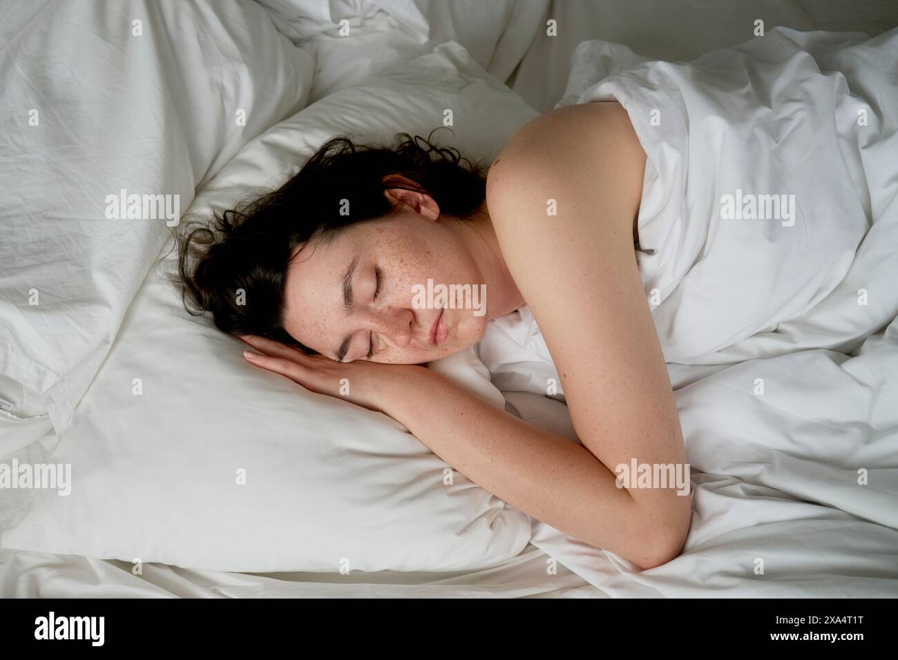 A woman sleeping peacefully in a white bed with her head resting on a ...