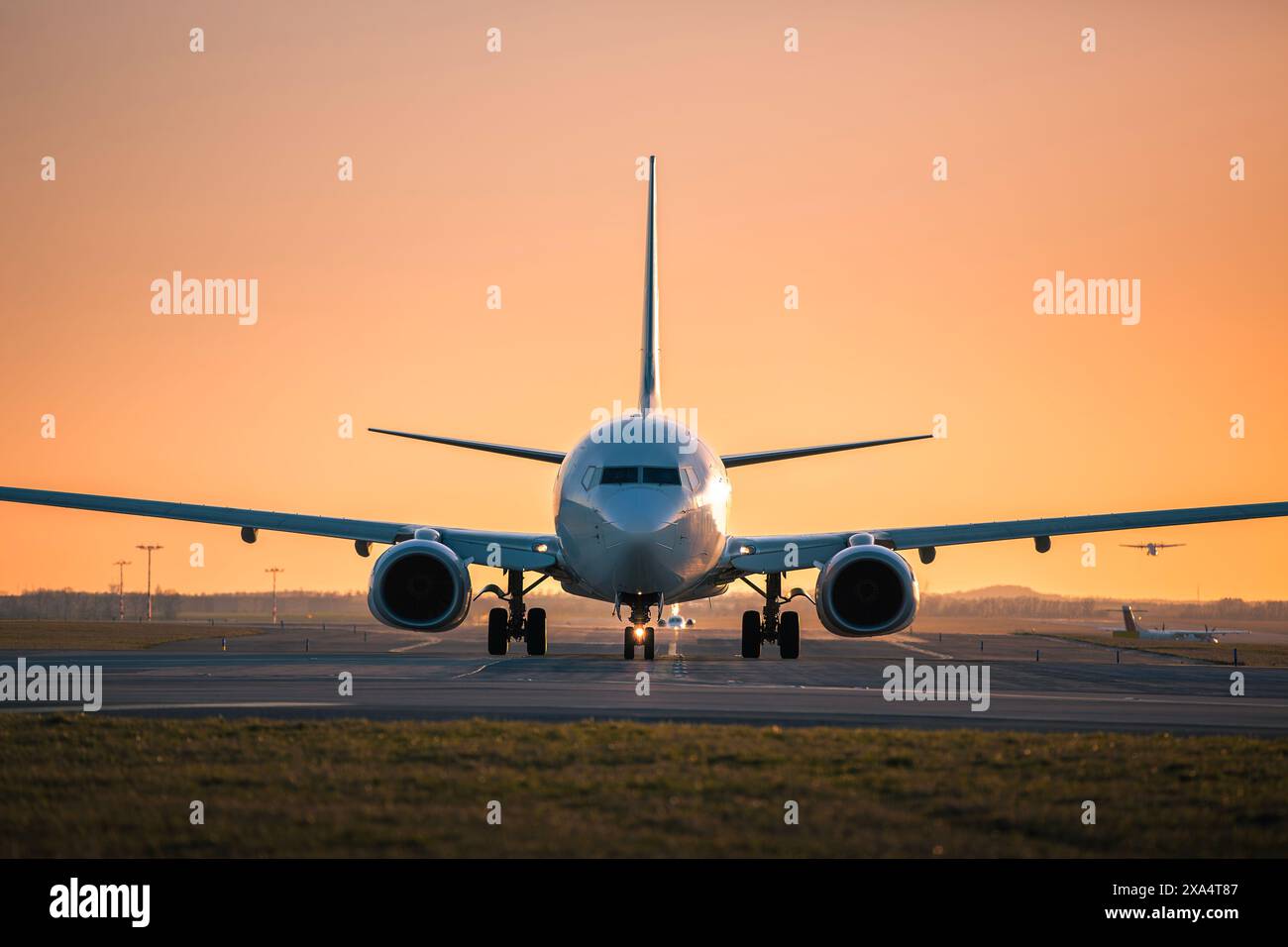Traffic at airport at golden sunset. Front view of taxiing airplane while other taking off from ...