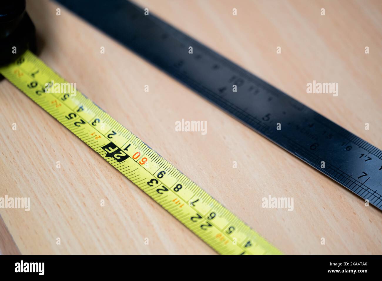 A close-up of a yellow and black tape measure extended on a wooden desk ...