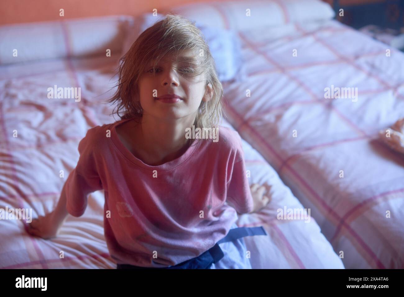Young child with messy hair sitting on a bed with a pink and white ...