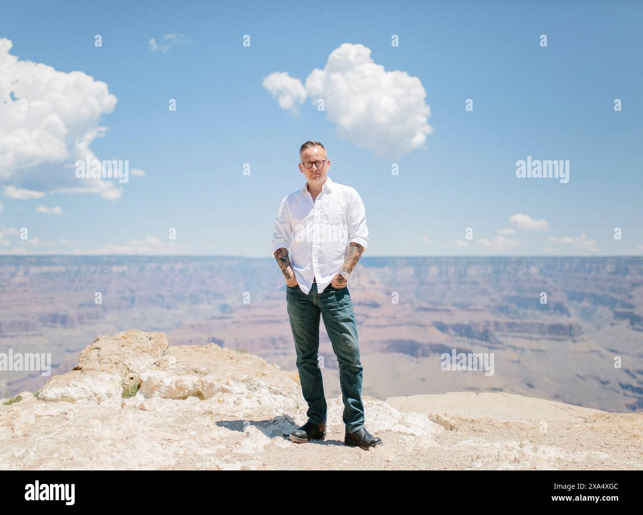 Smiling man standing at the edge of the Grand Canyon with clear blue ...