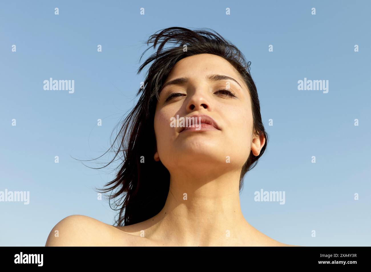 Woman with windblown hair gazing confidently against a clear sky ...