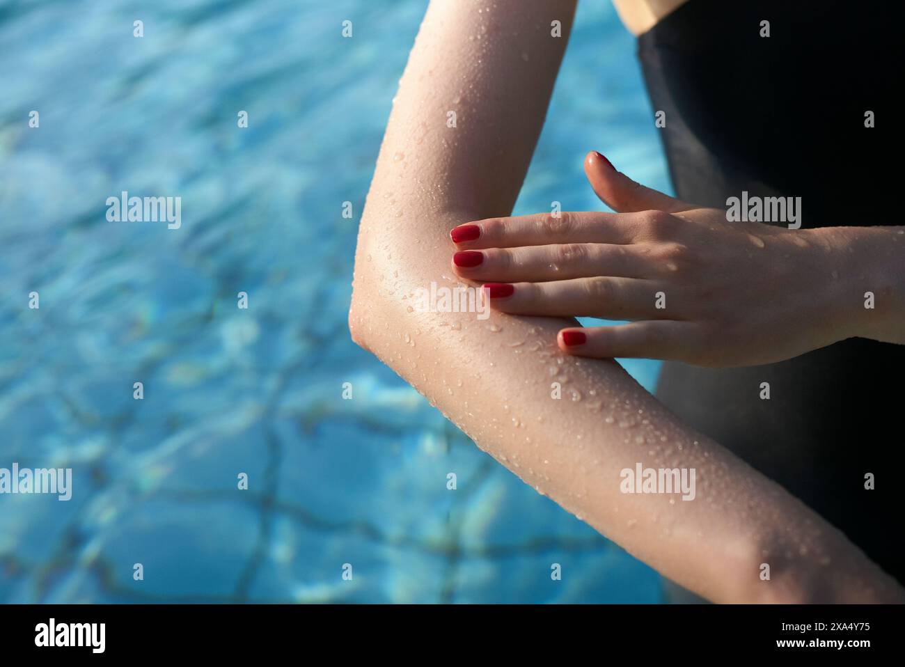 A person applies sunscreen on their arm beside a swimming pool with ...