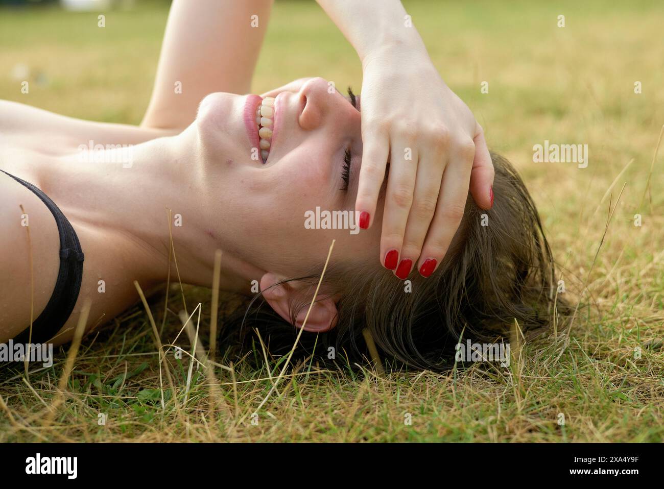 Woman laughing while lying on the grass with one hand over her eyes ...