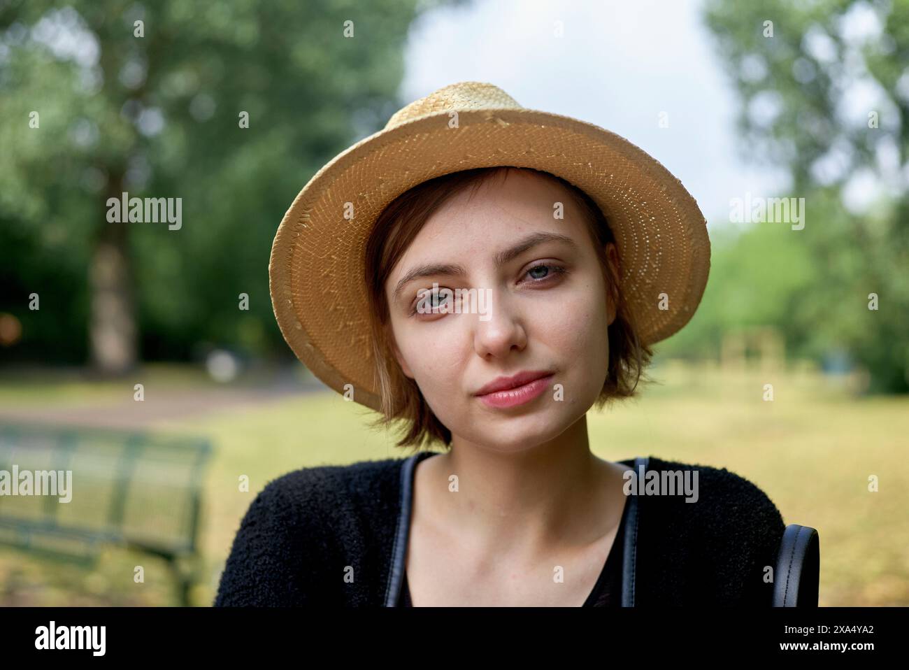 A young woman with short hair wearing a straw hat smiles subtly in a ...