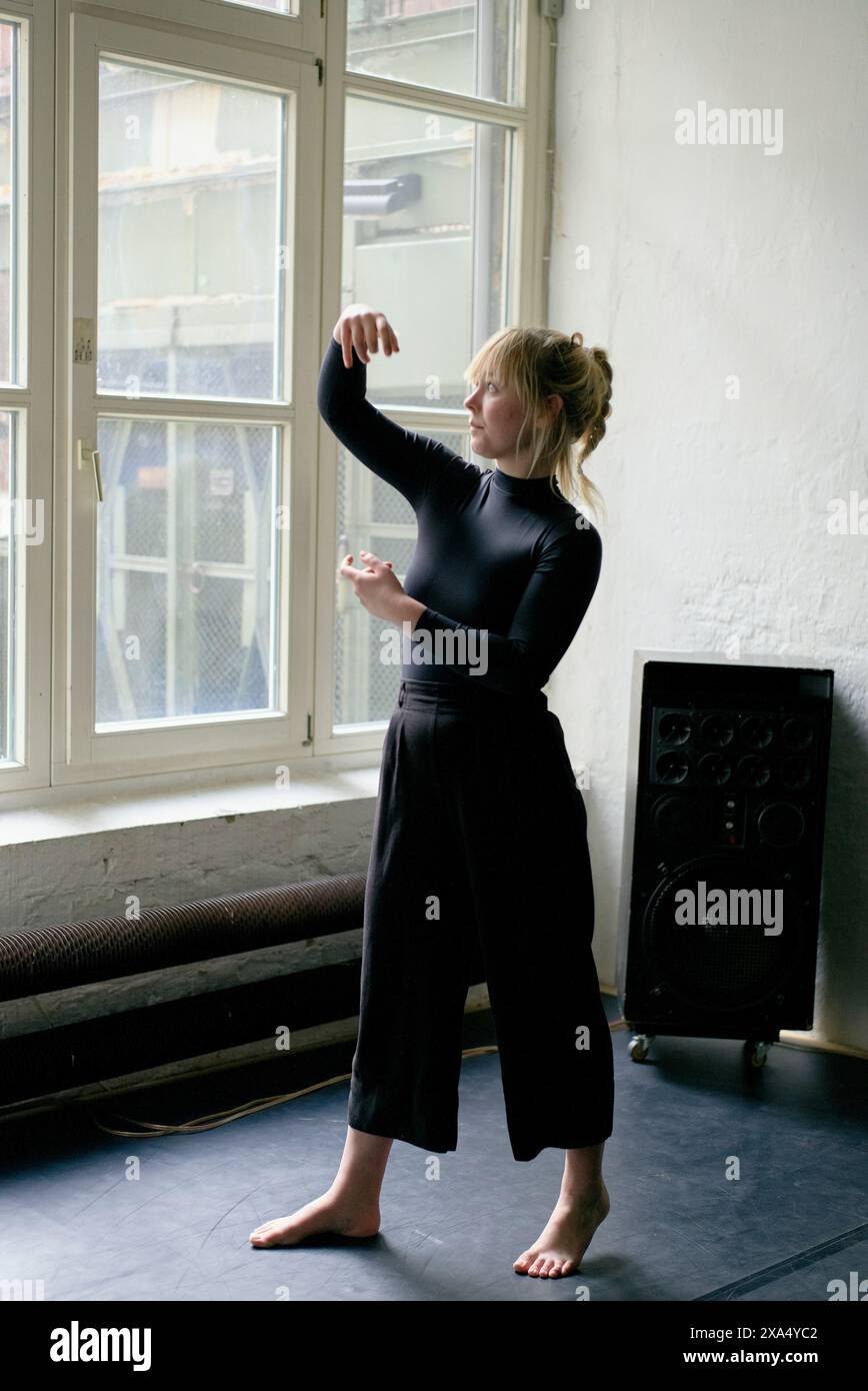 A focused woman practicing ballet moves by a window in a studio Stock ...