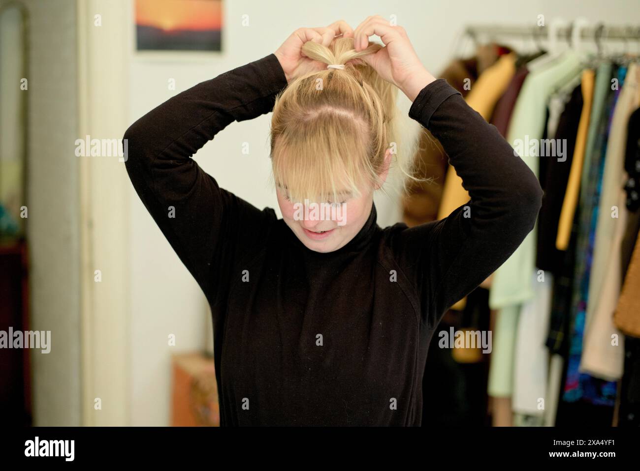 Woman tying her hair in a ponytail with a backdrop of clothes hanging ...