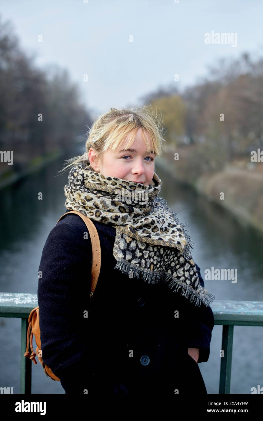 Woman in a leopard print scarf leaning on a bridge railing with a river ...