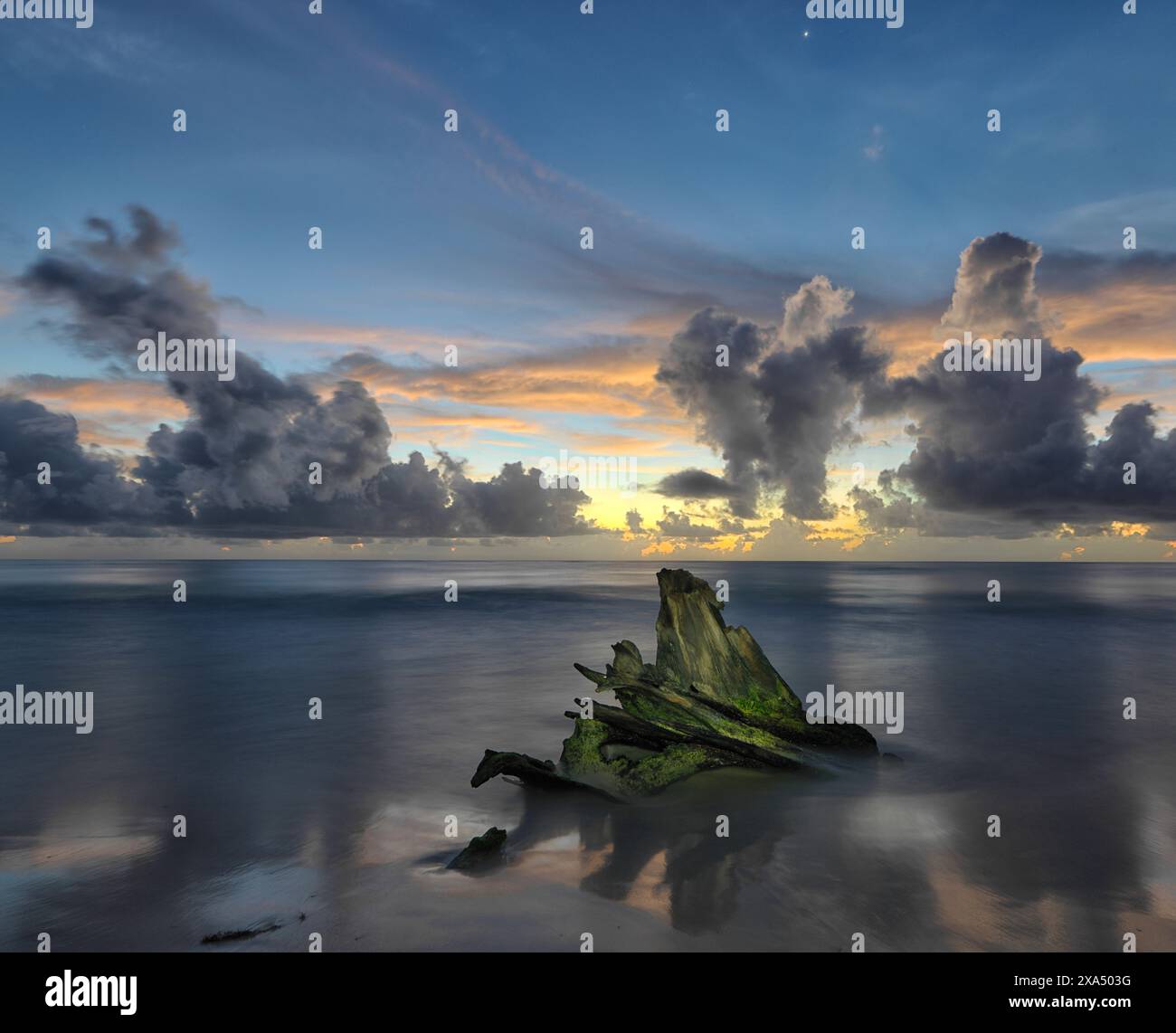 Sunrise colors the skies over a tranquil sea with a mossy, weathered ...