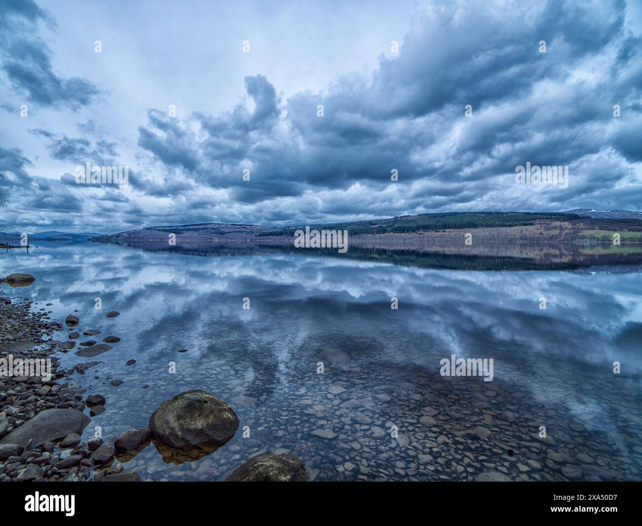Serene lake with dramatic cloud reflections and a pebble shoreline ...