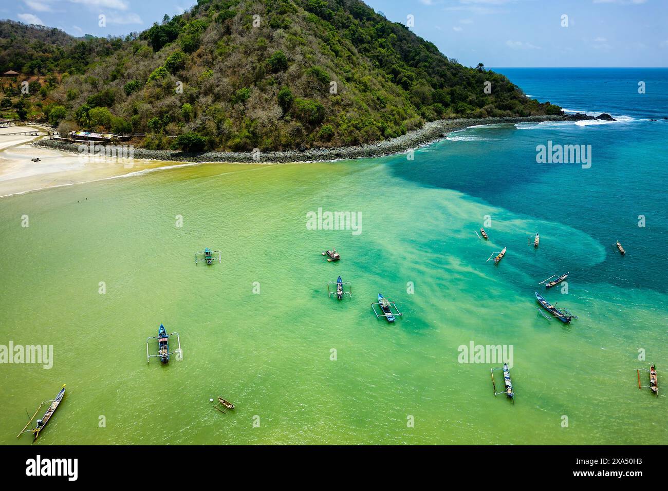 Traditional outrigger style boats in a warm, muddy ocean in Lombok ...