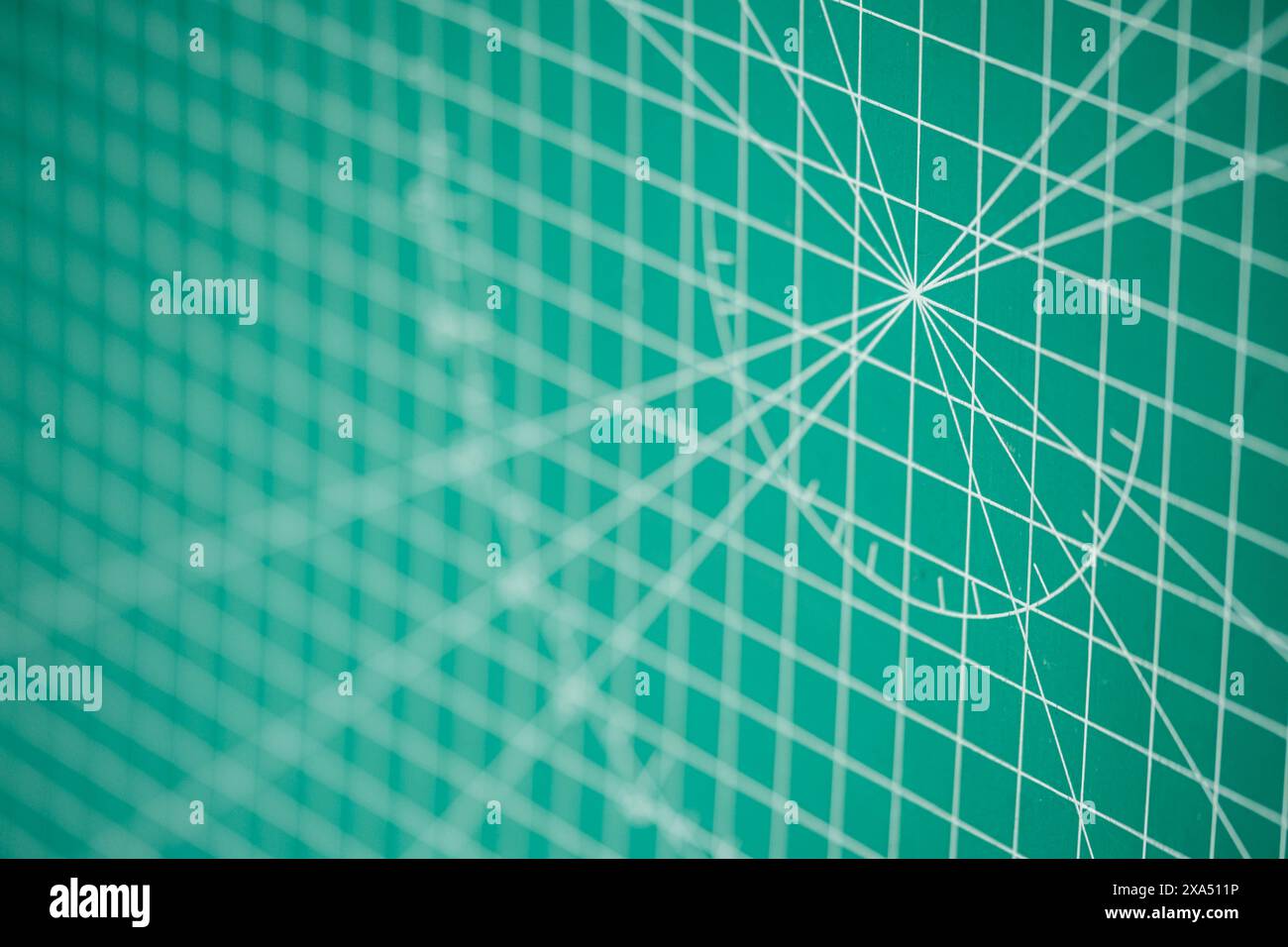 Close-up of a green cutting mat with white grid lines and geometric ...