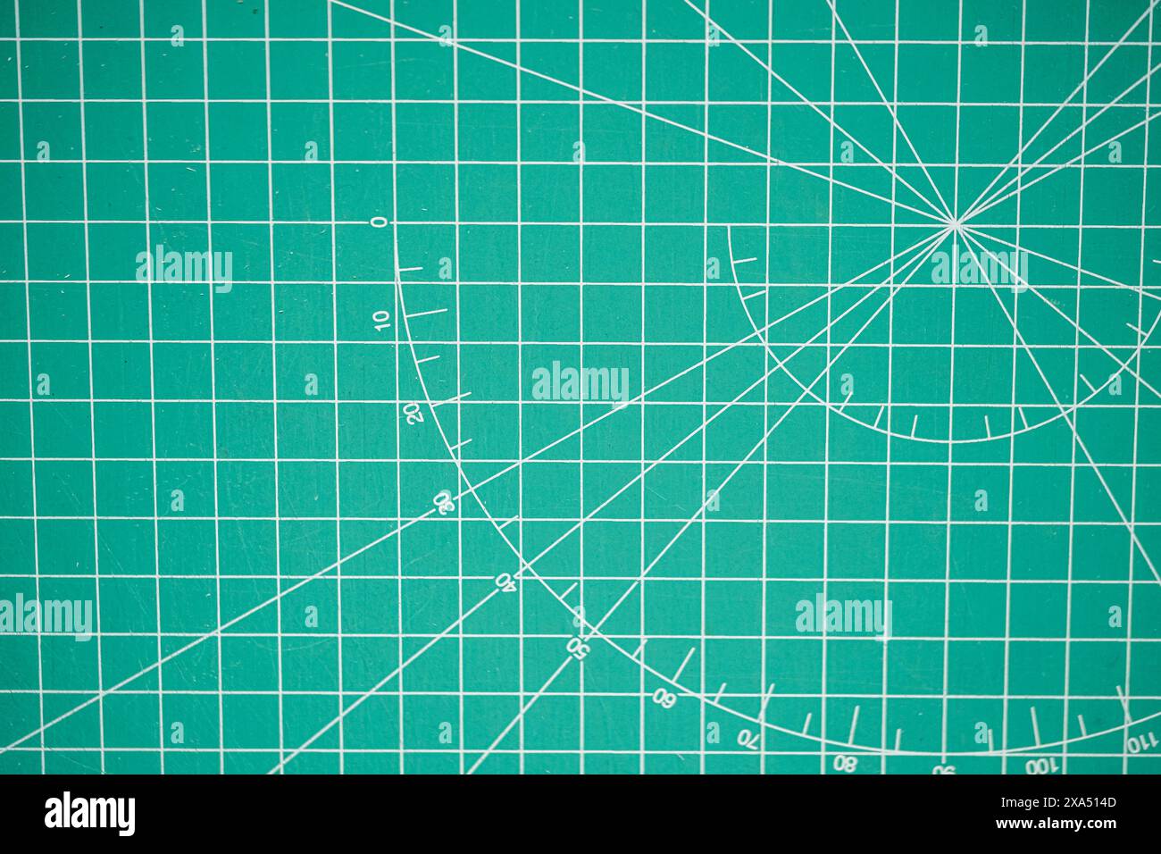 Close-up of a green cutting mat with white grid lines and geometric ...