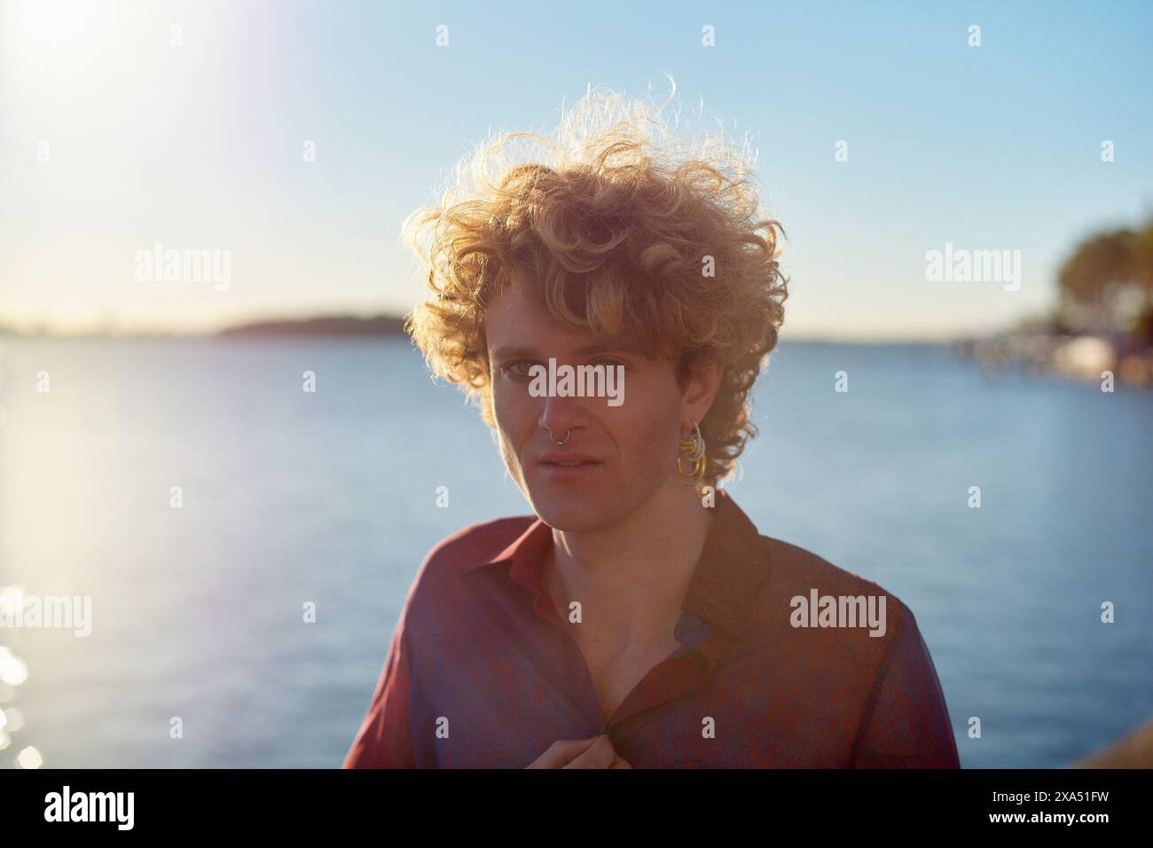 Sunlit portrait of a curly-haired person by the water during golden ...