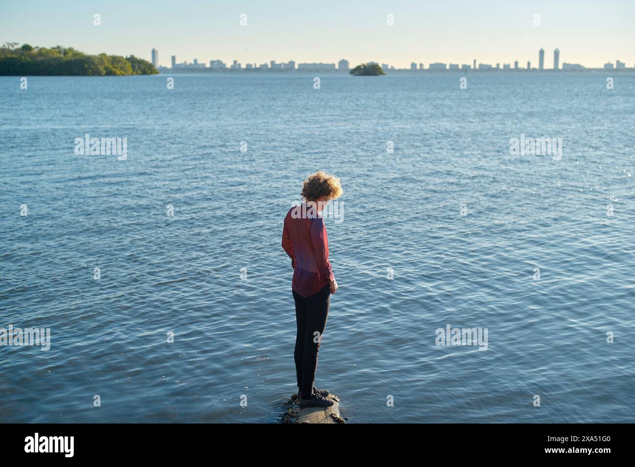 Woman standing on a rock at the edge of a calm lake gazing towards the ...