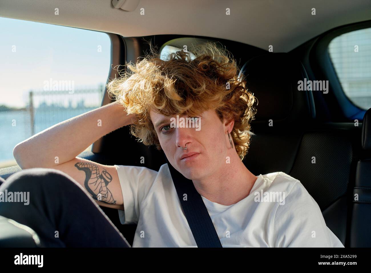 Curly-haired young man sitting in a car with a bridge in the background ...