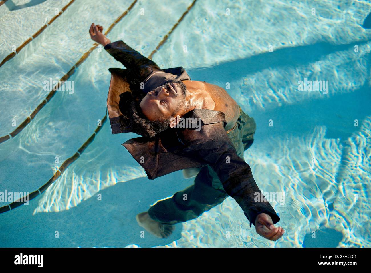 Man floating peacefully in a clear blue swimming pool, with sunlight ...