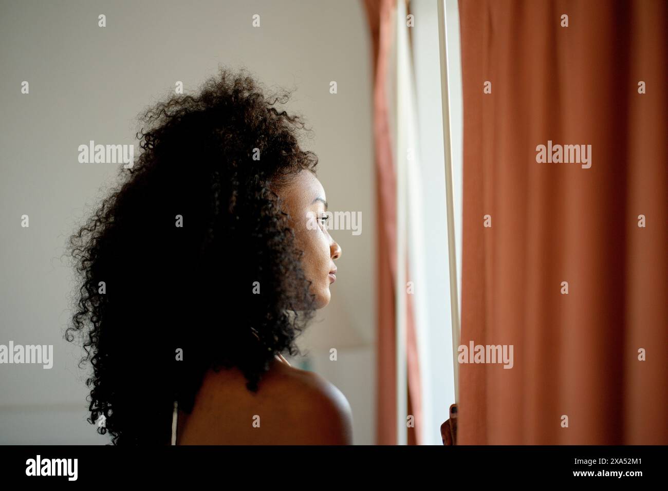Young woman with curly hair looking out a window with a serene ...