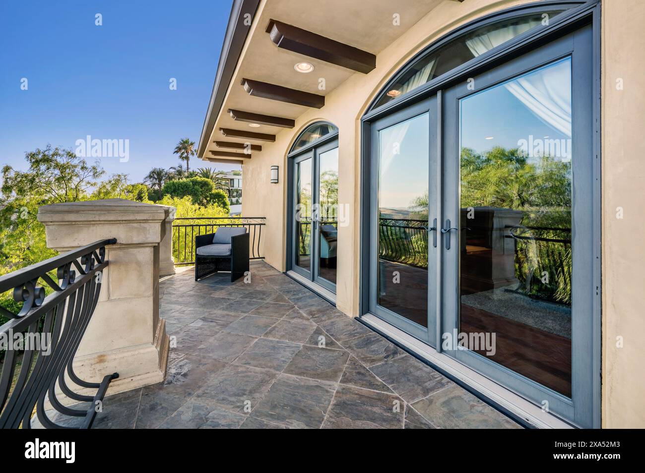 Stone patio with black iron railing, chair, and trees visible from ...