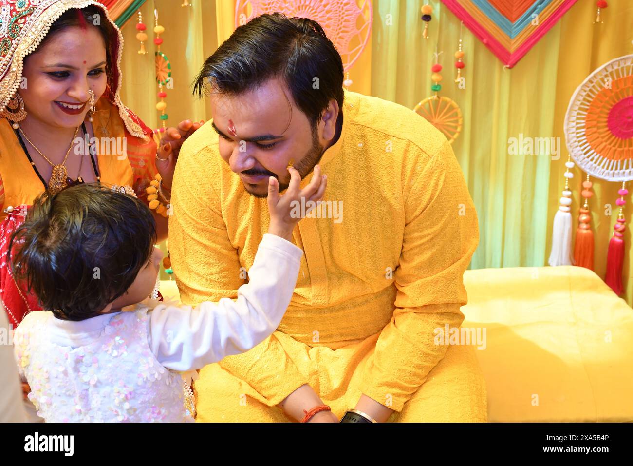 A man seated beside a young girl and an adult in Haldi ceremony Stock ...
