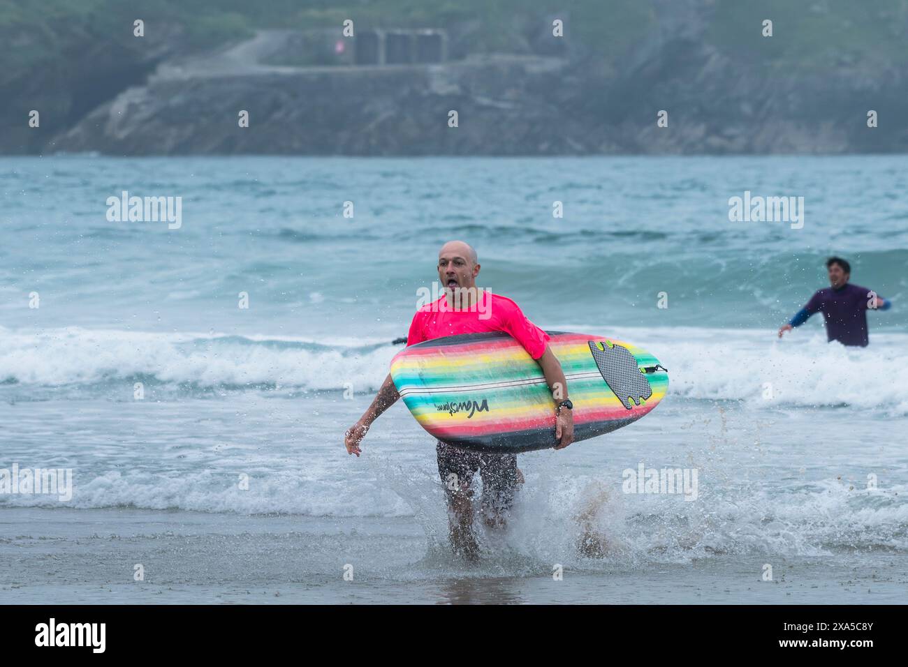 A surfer carrying his surfboard running out of the sea after competing ...