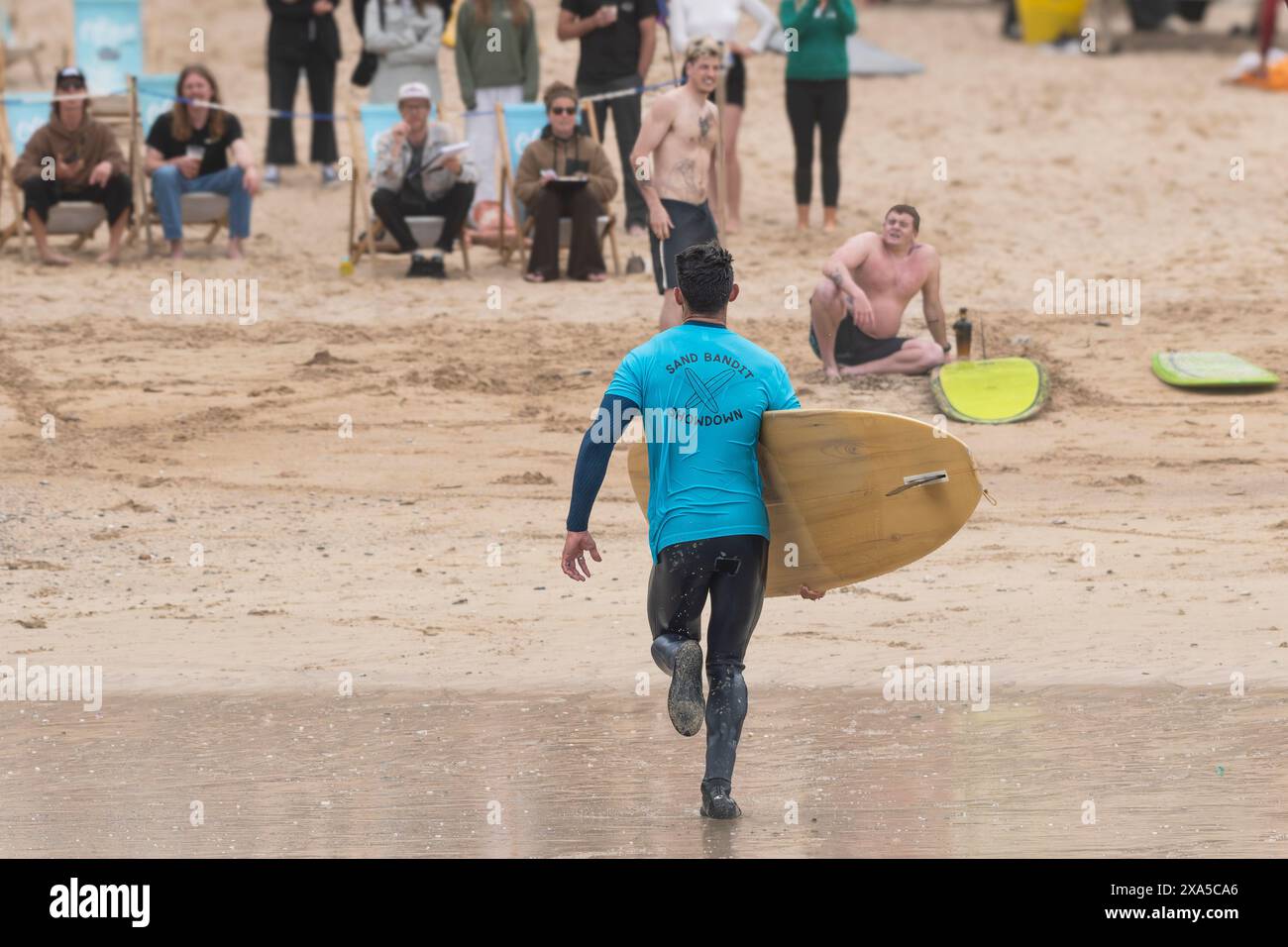 A surfer carrying his surfboard running out of the sea after competing ...