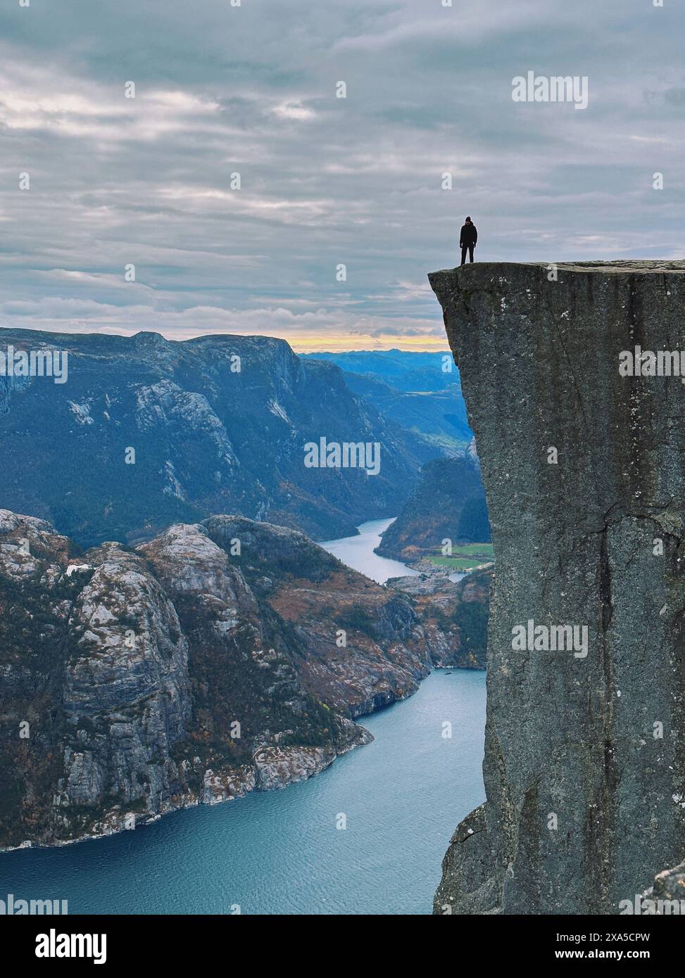 A man standing on a high cliff admiring a lake below Stock Photo - Alamy