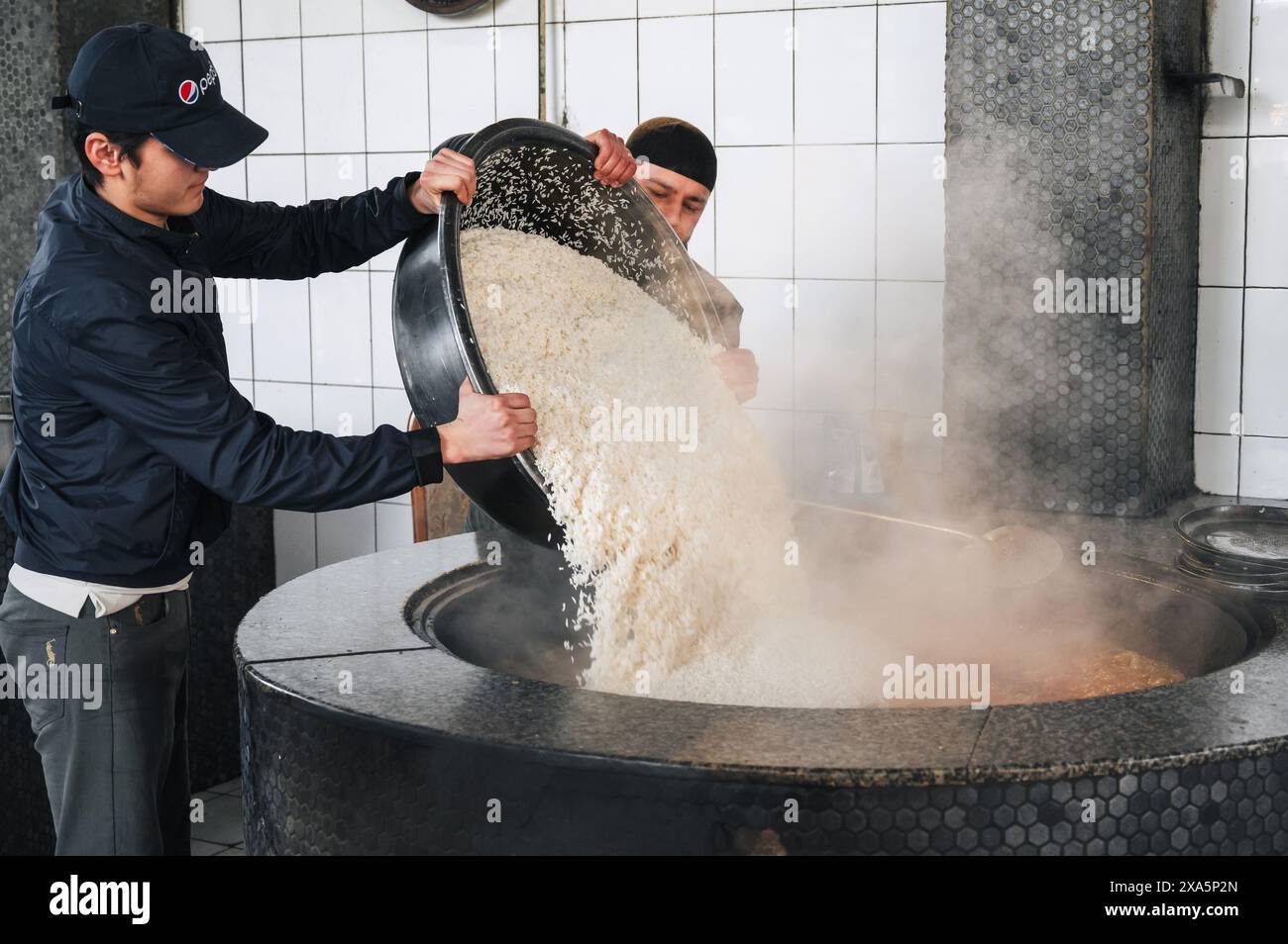male chefs pour rice for traditional Uzbek pilaf into a cauldron in ...