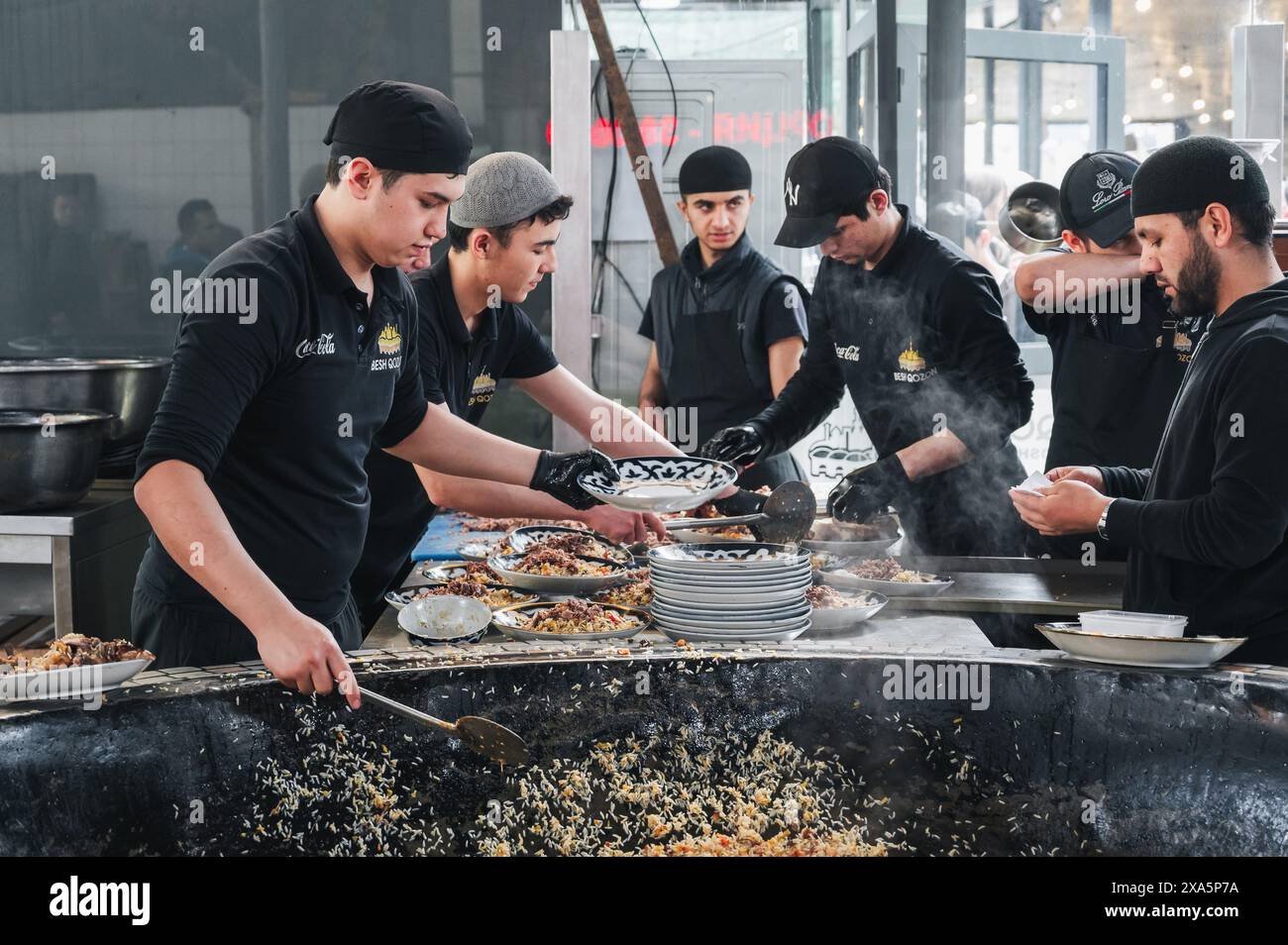 male cooks put ready-made traditional Uzbek pilaf from a cauldron on ...