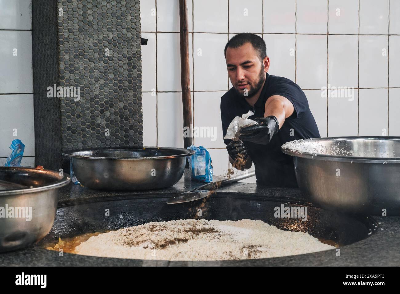 male cook seasons rice with cumin for traditional Uzbek pilaf in a ...
