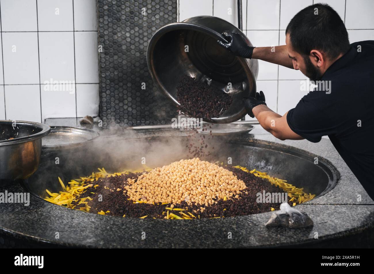 male cook adds barberry to a cauldron with carrots and chickpeas to ...