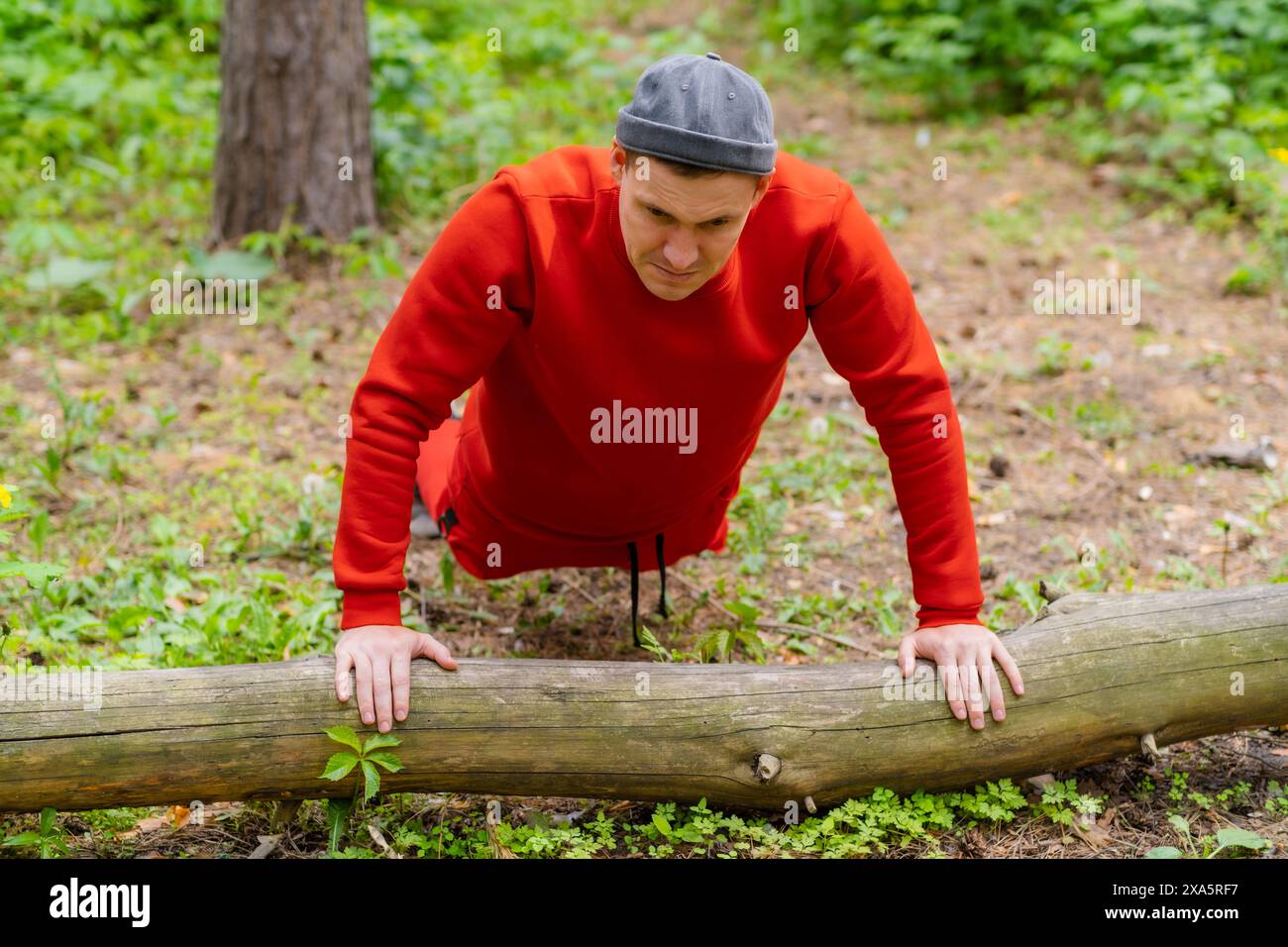 A man performs push-ups using the log as support. The backdrop is a ...