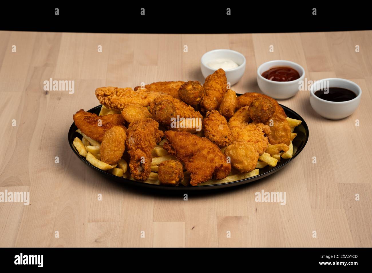 A close-up of chicken wings and fries served on a black plate with ...
