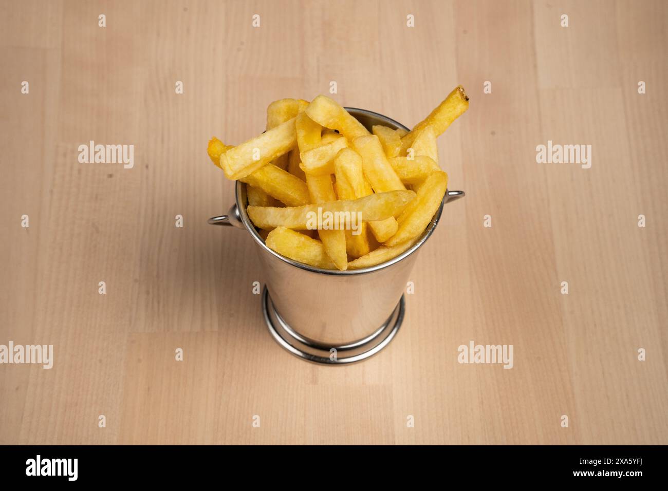 A top view of crispy fries in a metal pail, set on a rustic wooden ...