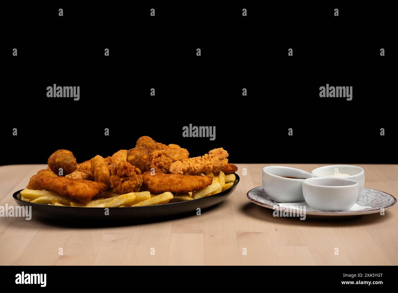 A close-up of chicken wings and fries served on a black plate with ...